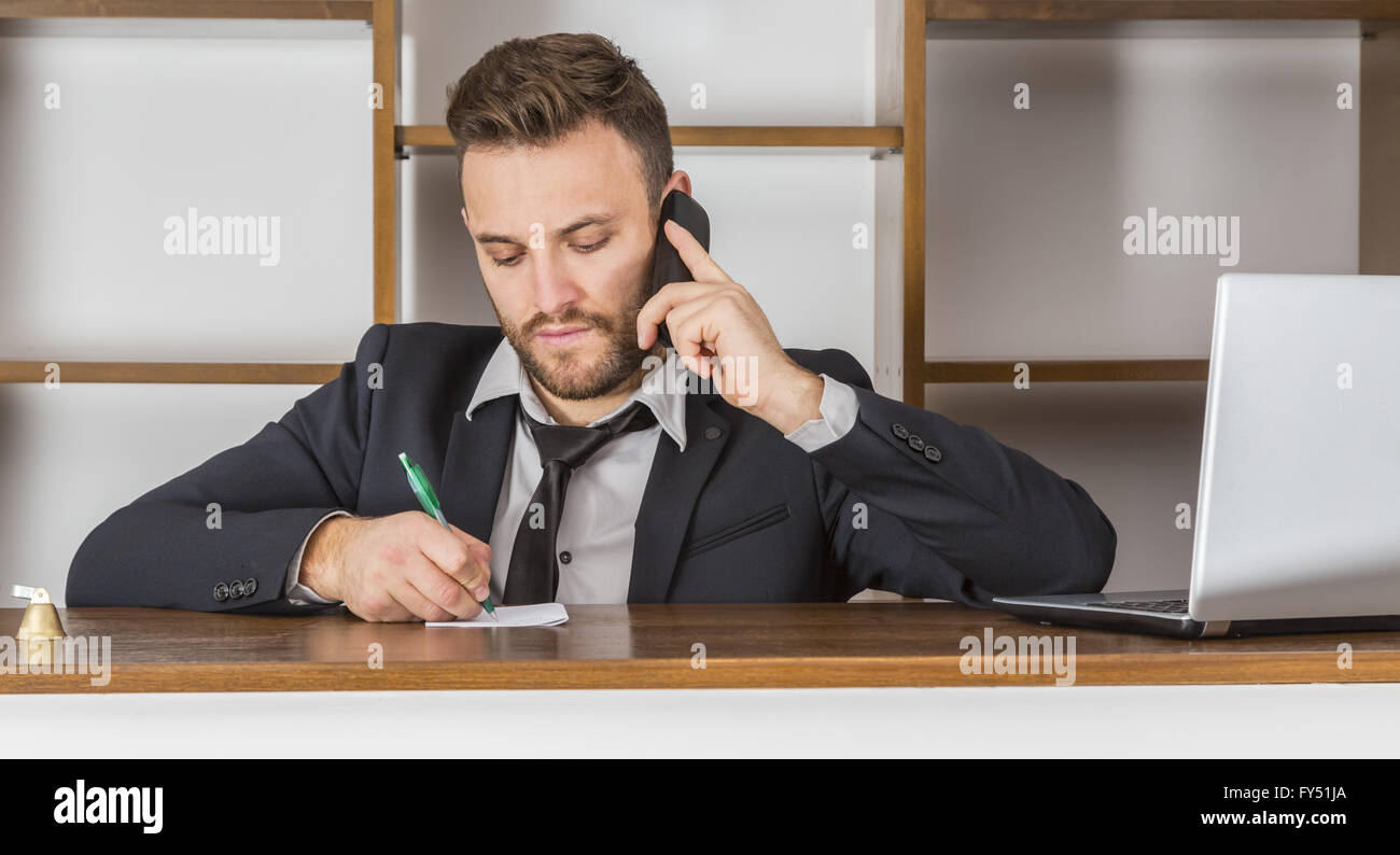 Portrait of a receptionist taking notice on a piece of paper while he ...