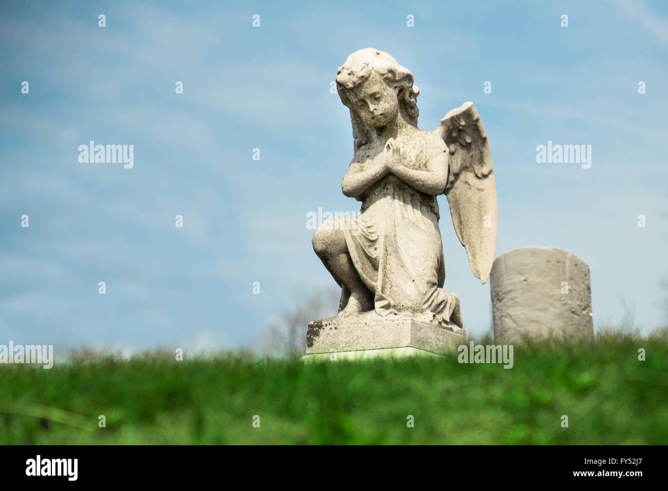 Praying angel statue with headstone in the background at cemetery Stock ...