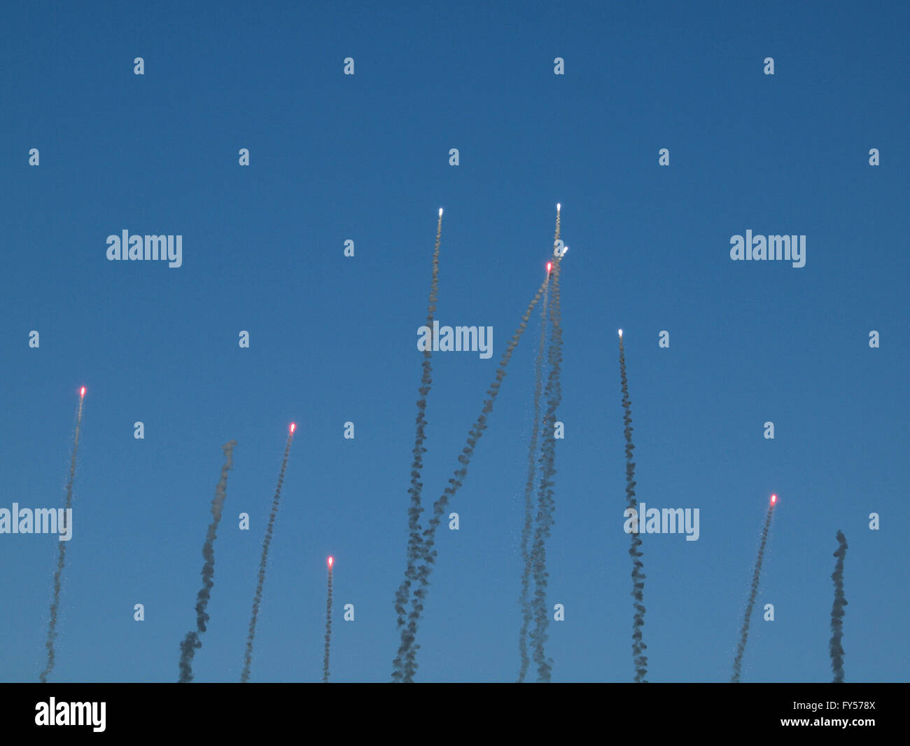 Red Fireworks soar into the air trailed by smoke during the day against ...