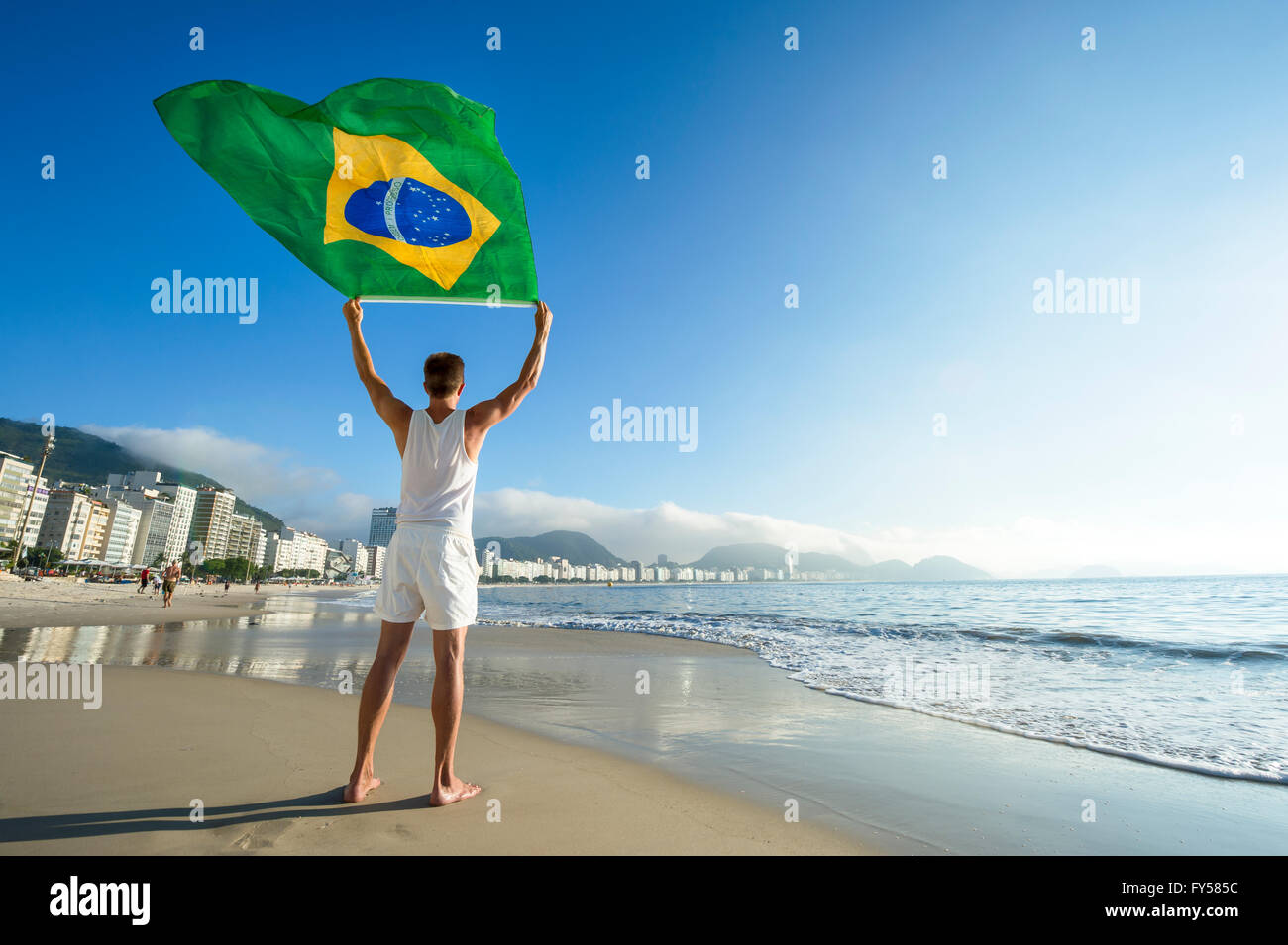 Athlete in white outfit standing with Brazilian flag waving in the wind ...
