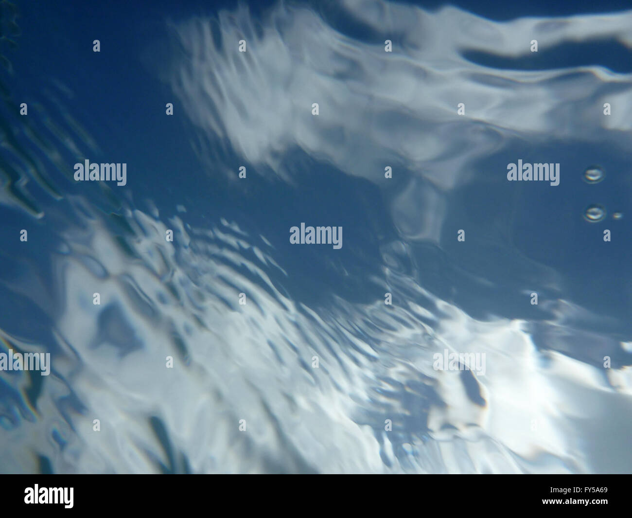 Looking through ocean water at blue sky and clouds with water ripples ...