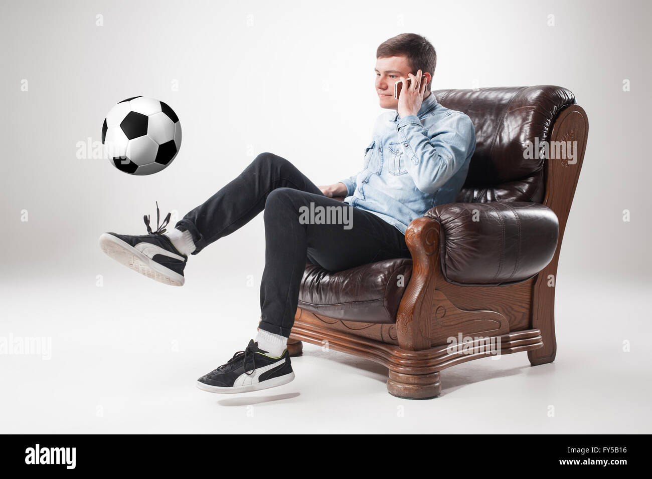 The portrait of fan with ball, holding tv remote on white background ...