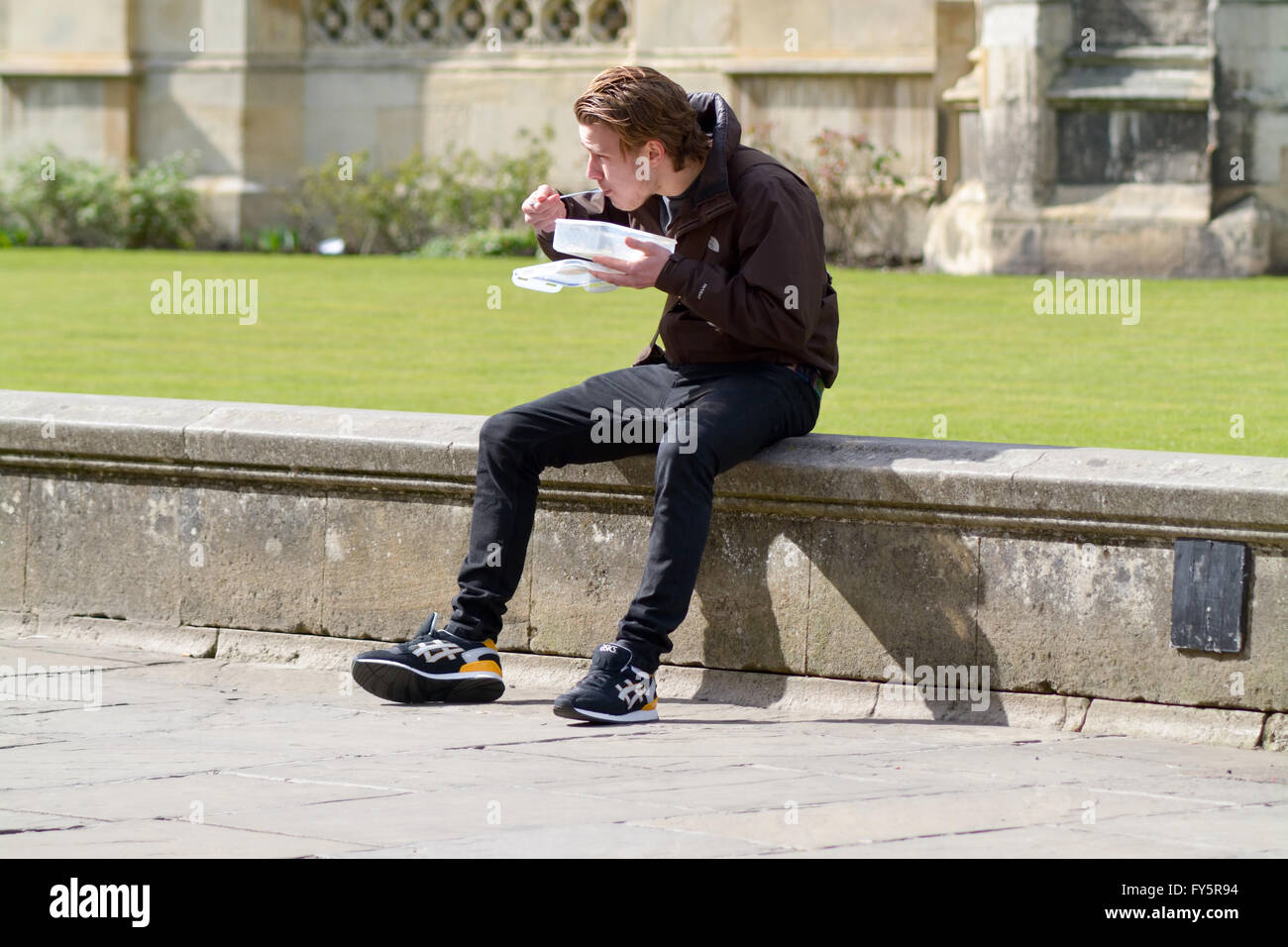 Young man sat on wall eating takeaway meal outside Corpus Christi ...