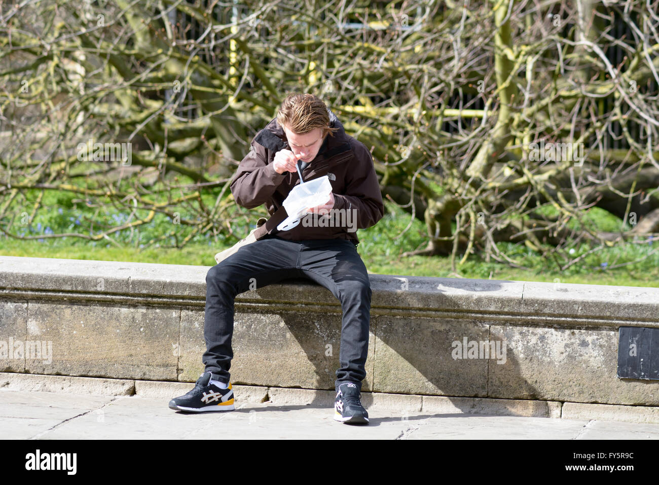 Young man sat on wall eating takeaway meal outside Corpus Christi ...
