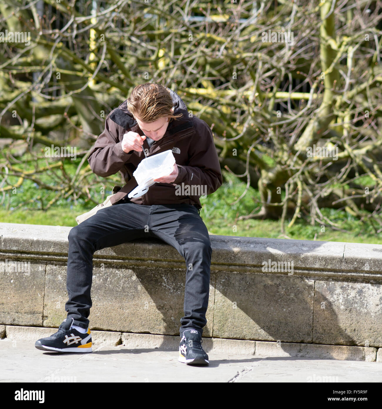 Young man sat on wall eating takeaway meal outside Corpus Christi ...