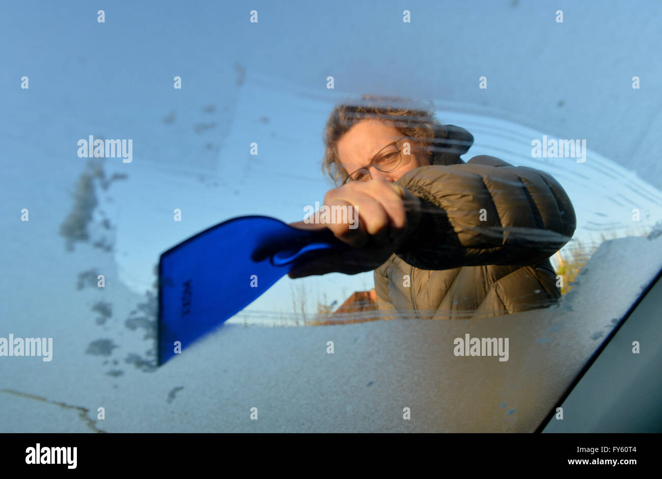 A woman is scratching the ice of the glass windshield of her car ...