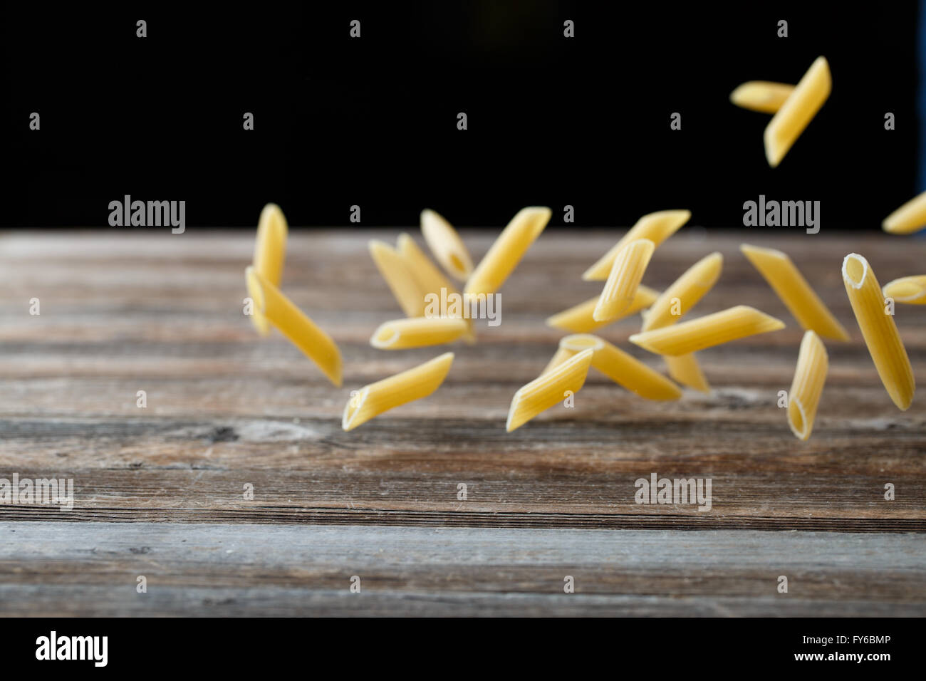 Falling penne pasta. Flying yellow raw macaroni over black background ...
