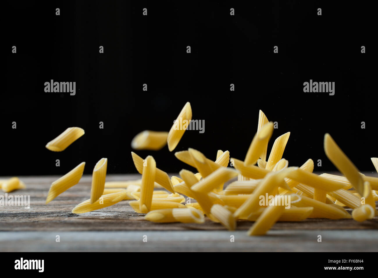 Falling penne pasta. Flying yellow raw macaroni over black background ...