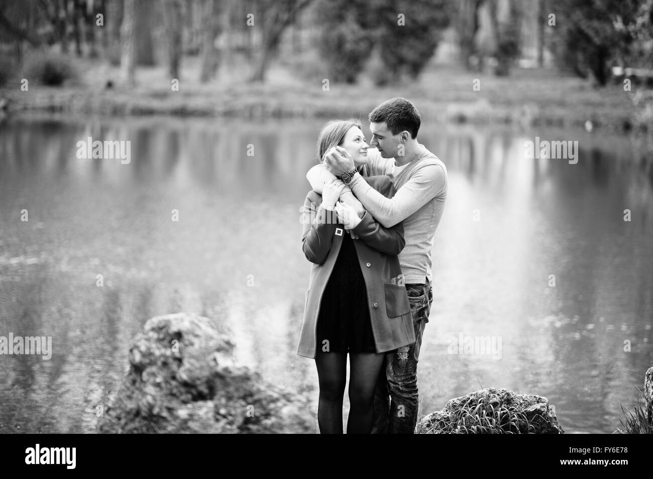 Happy loving couple stay and hugging at park background lake. Black and ...