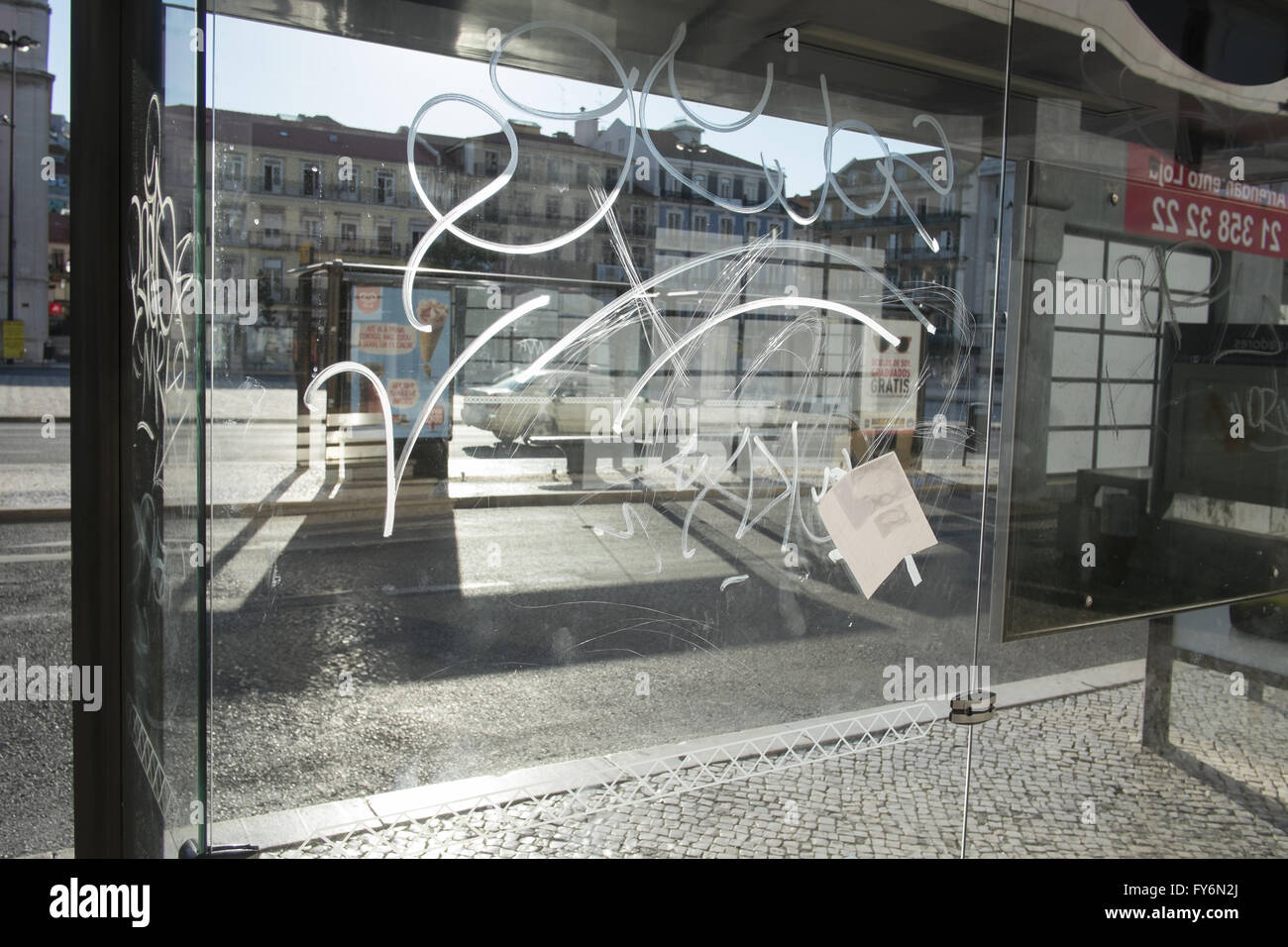 A perspex bus shelter is etched with grafiti. The early morning sun ...