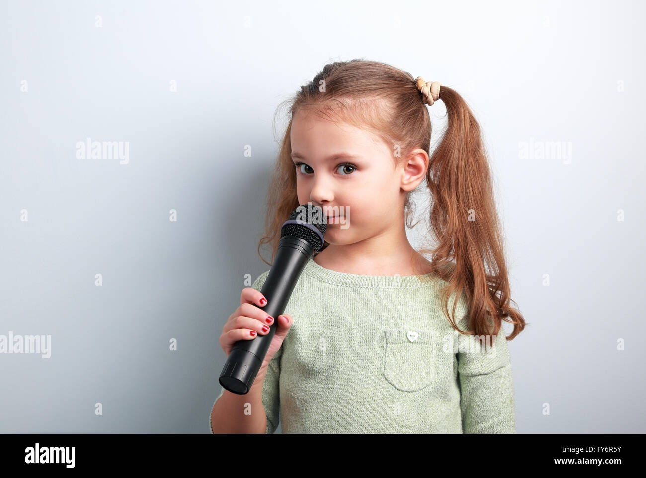 Cute fun kid girl singing song in microphone on blue background. Young ...