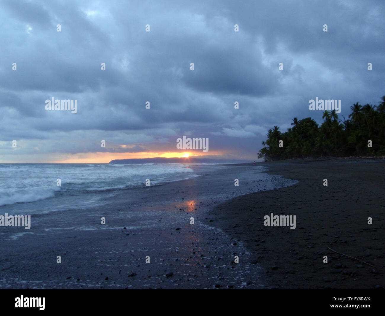 Sunsets behind mountains as wave lap along the beach in Punta Banco ...