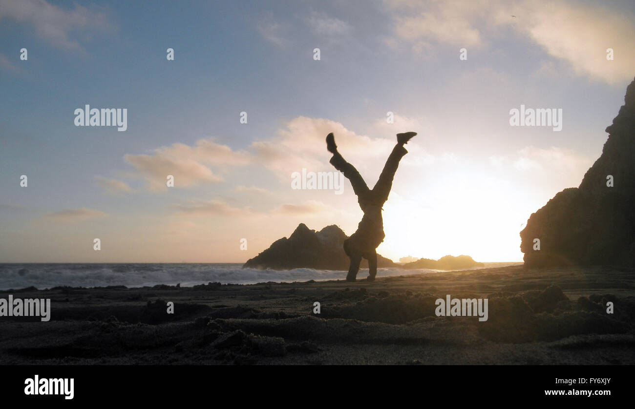 Man does handstand on the Ocean beach during a sunset splitting his ...