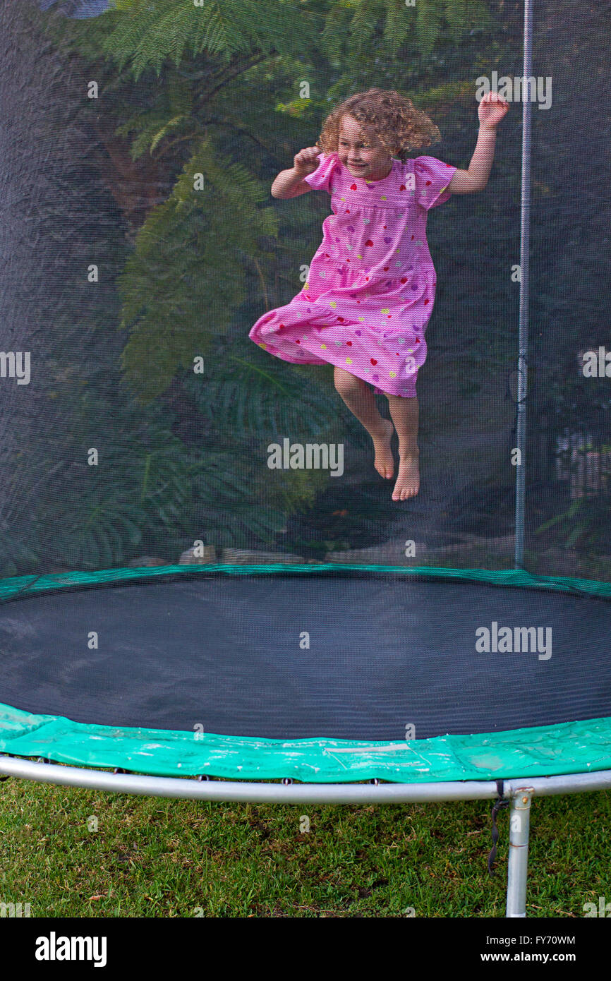 Young girl in pink dress jumping on trampoline Stock Photo - Alamy