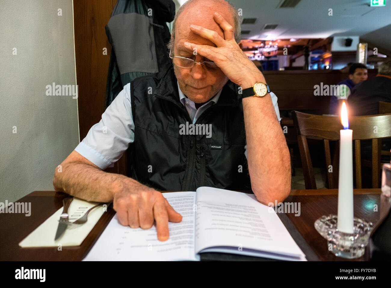 Senior man reading menu by candlelight in Vinolio Italian restaurant ...