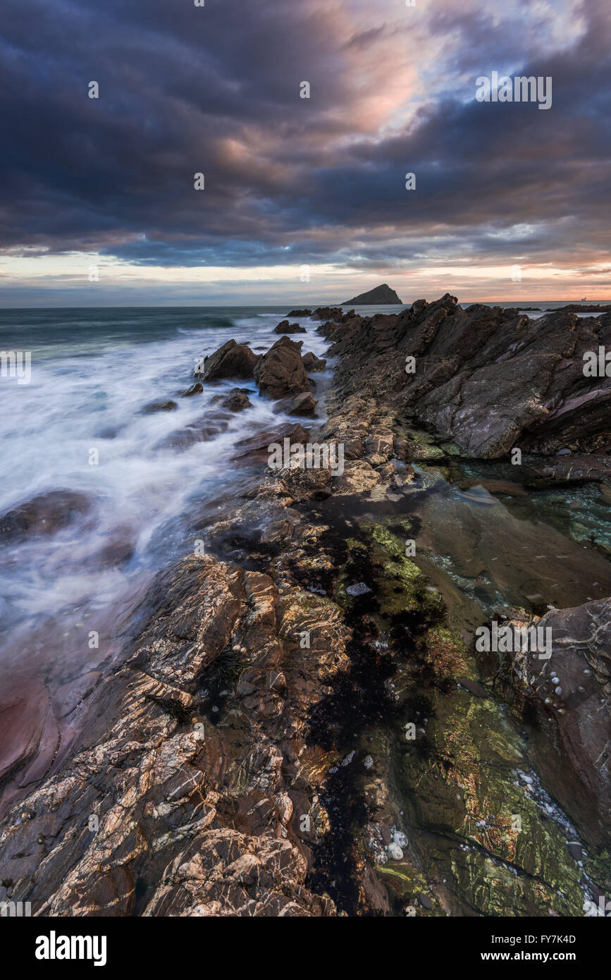 Red rocks on beach at sunset, dramatic clouds and waves Stock Photo - Alamy