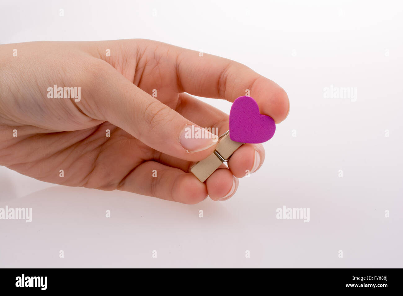 Hand holding a red clothespin with a heartshape on a white background ...
