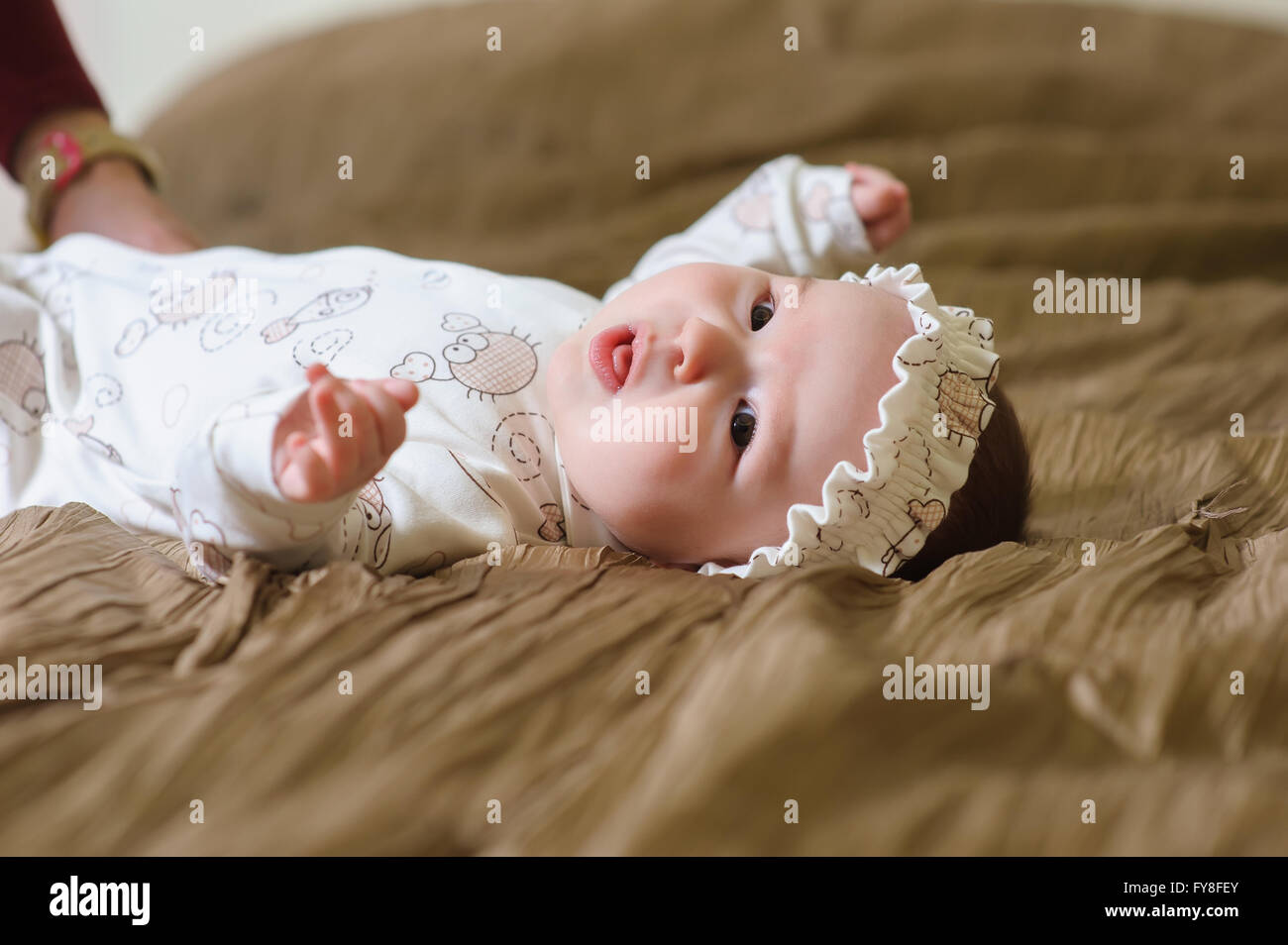 Baby girl lying on bed and grimacing Stock Photo - Alamy