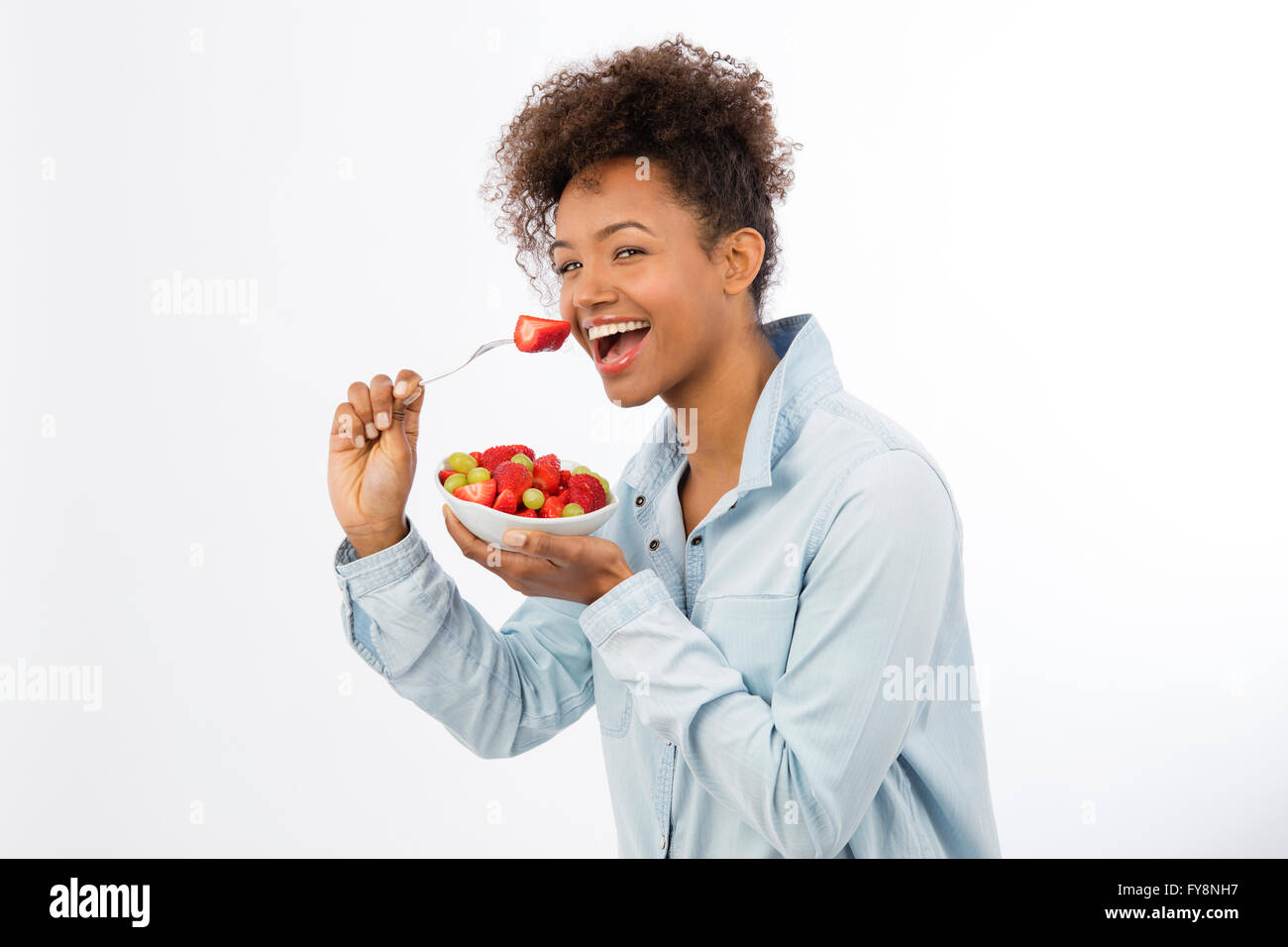 Portrait of happy young woman eating fruits in front of white ...