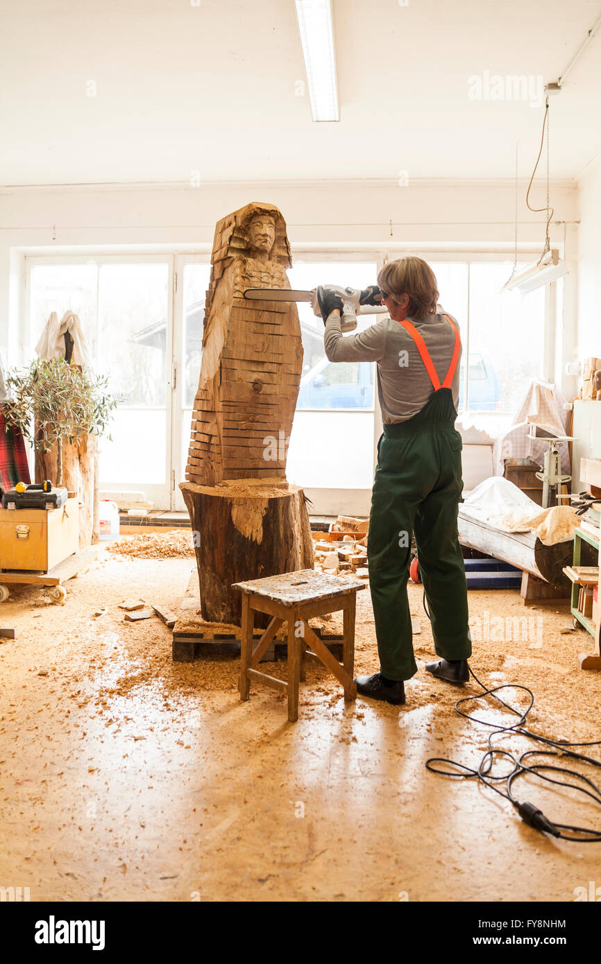 Wood carver in workshop working on sculpture with chainsaw Stock Photo ...