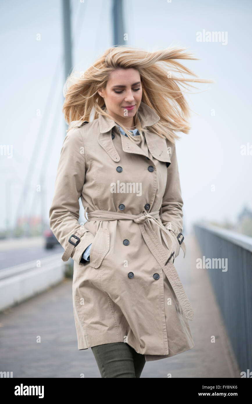 Portrait of young woman wearing trench coat walking on a bridge Stock ...