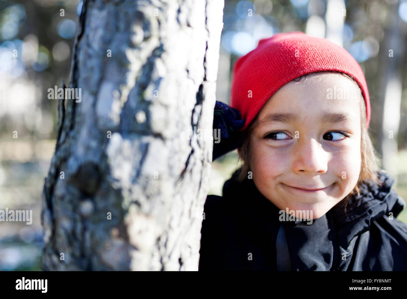 Portrait of smiling little boy hiding behind a tree trunk Stock Photo ...