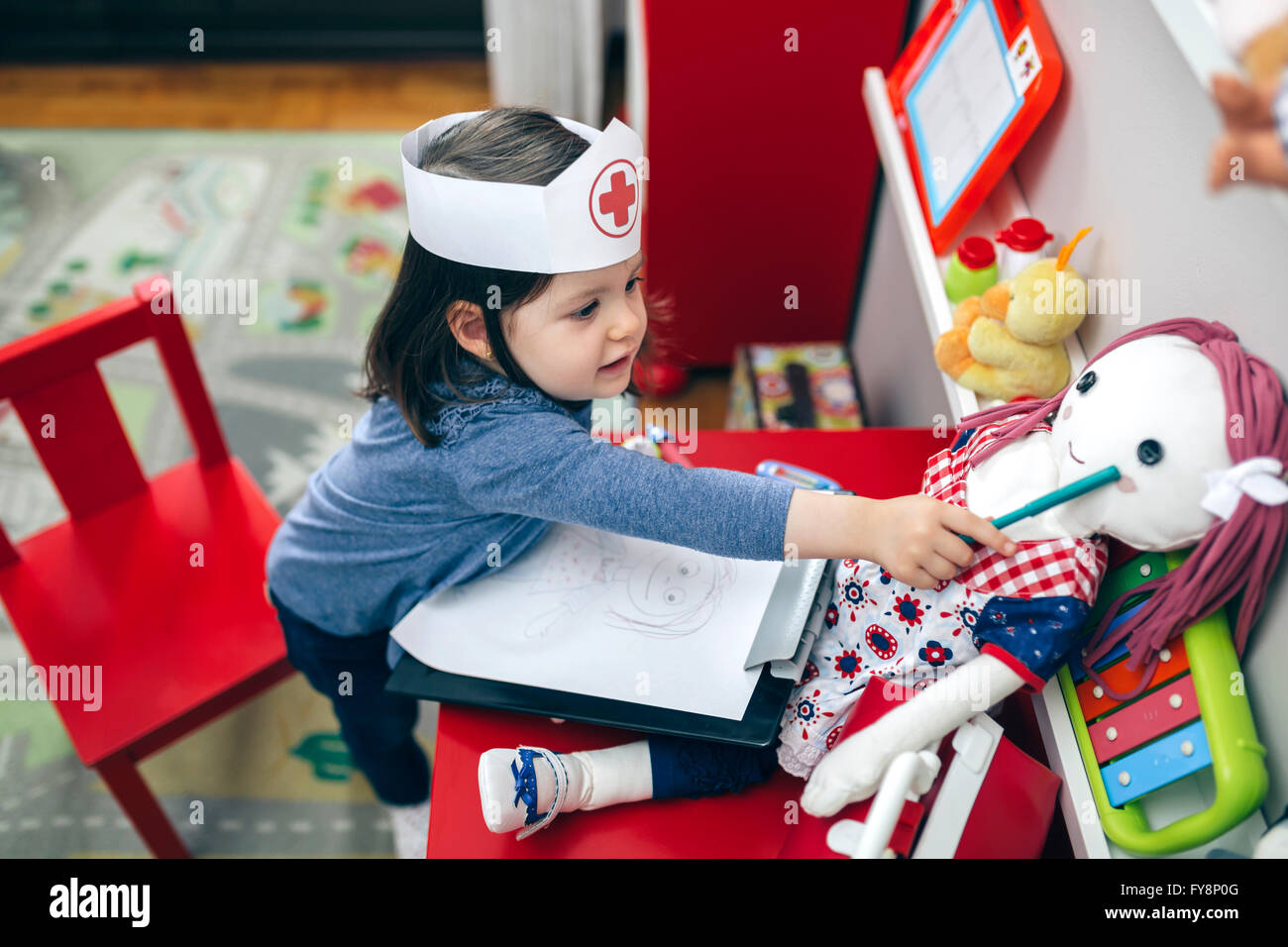 Little girl with nurse cap drawing her doll Stock Photo - Alamy