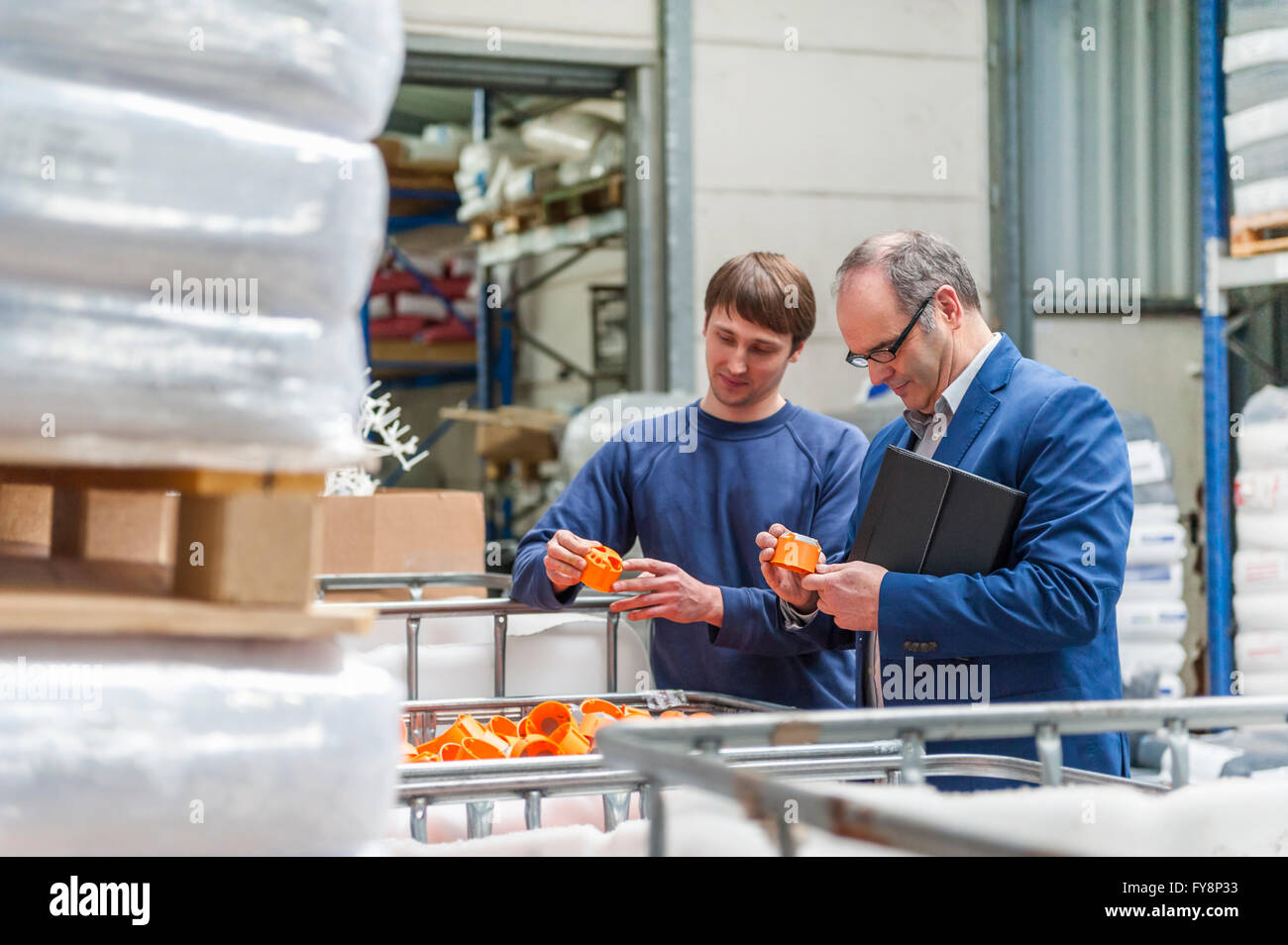 Manager and worker in storage of plastics factory checking products ...
