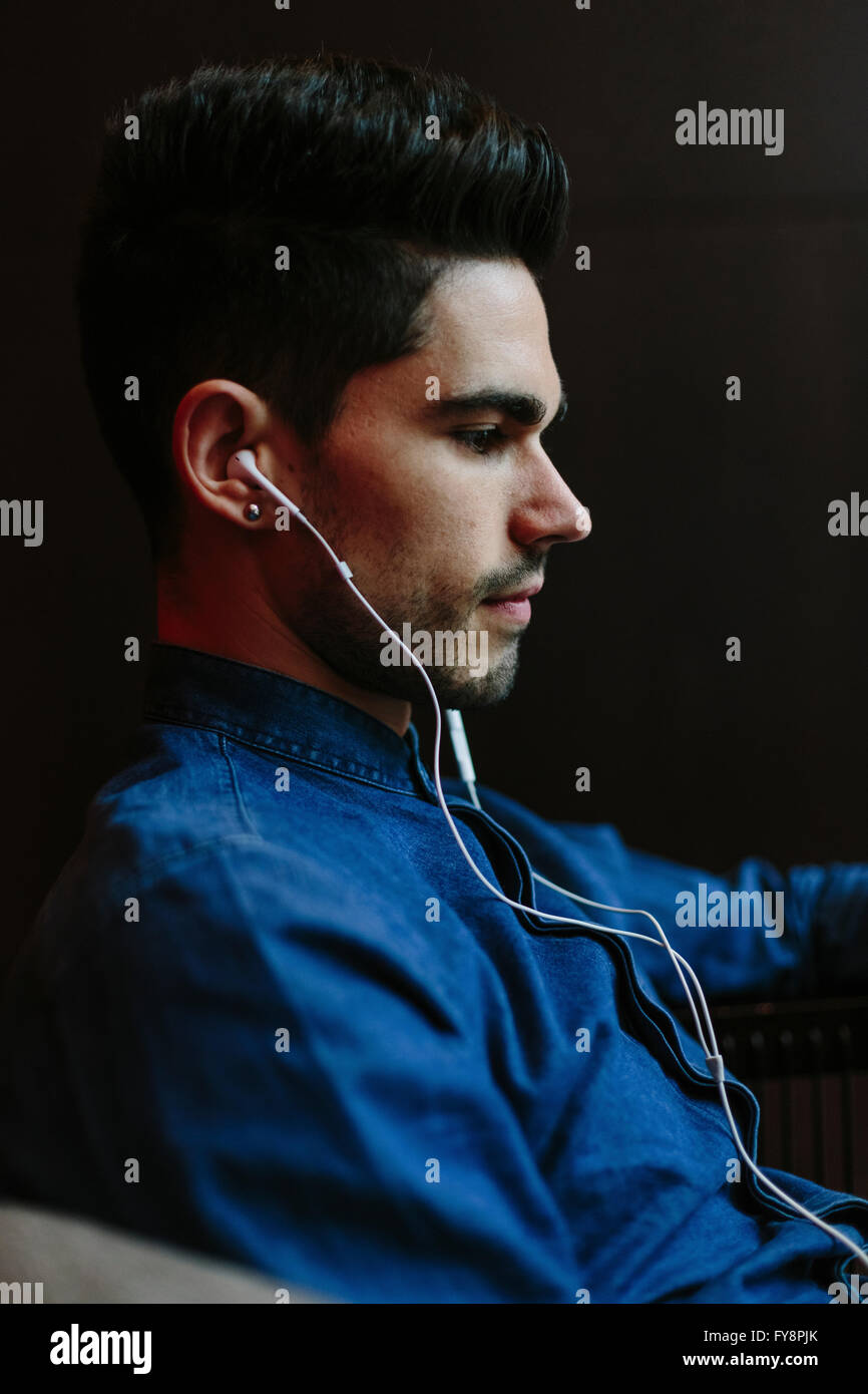 Profile of young man hearing music with earphones in front of black ...