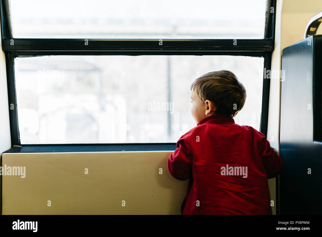 Back view of little boy on his first train ride looking through window ...