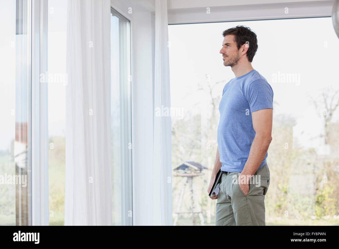 Man at home standing at window looking out Stock Photo - Alamy