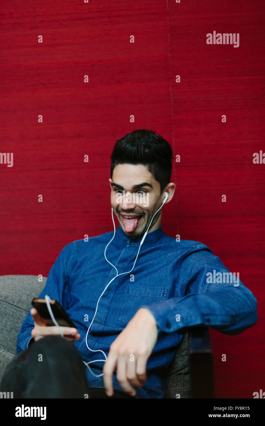 Young businessman sitting on armchair hearing music with earphones ...