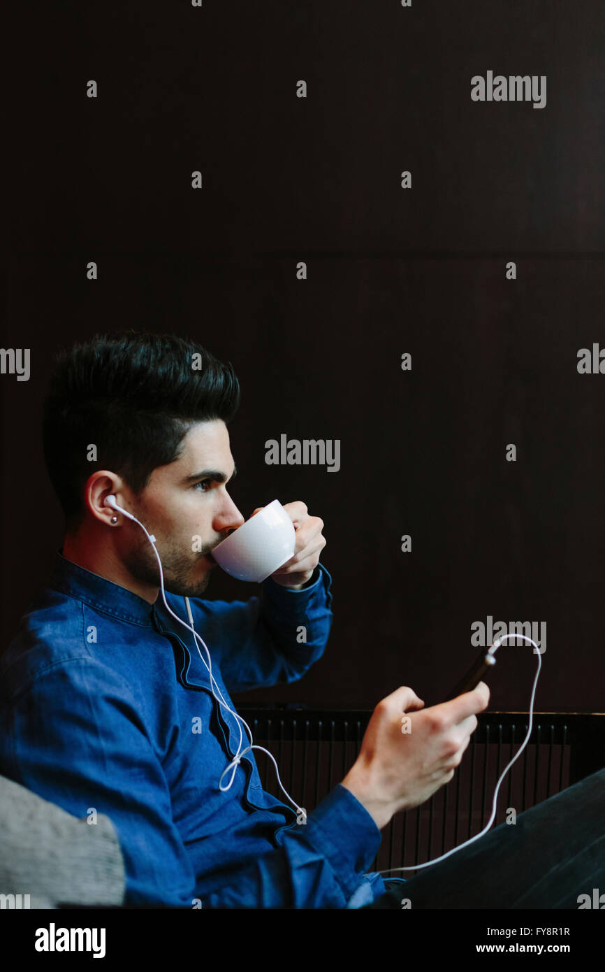 Profile of young man hearing music with earphones while drinking coffee ...