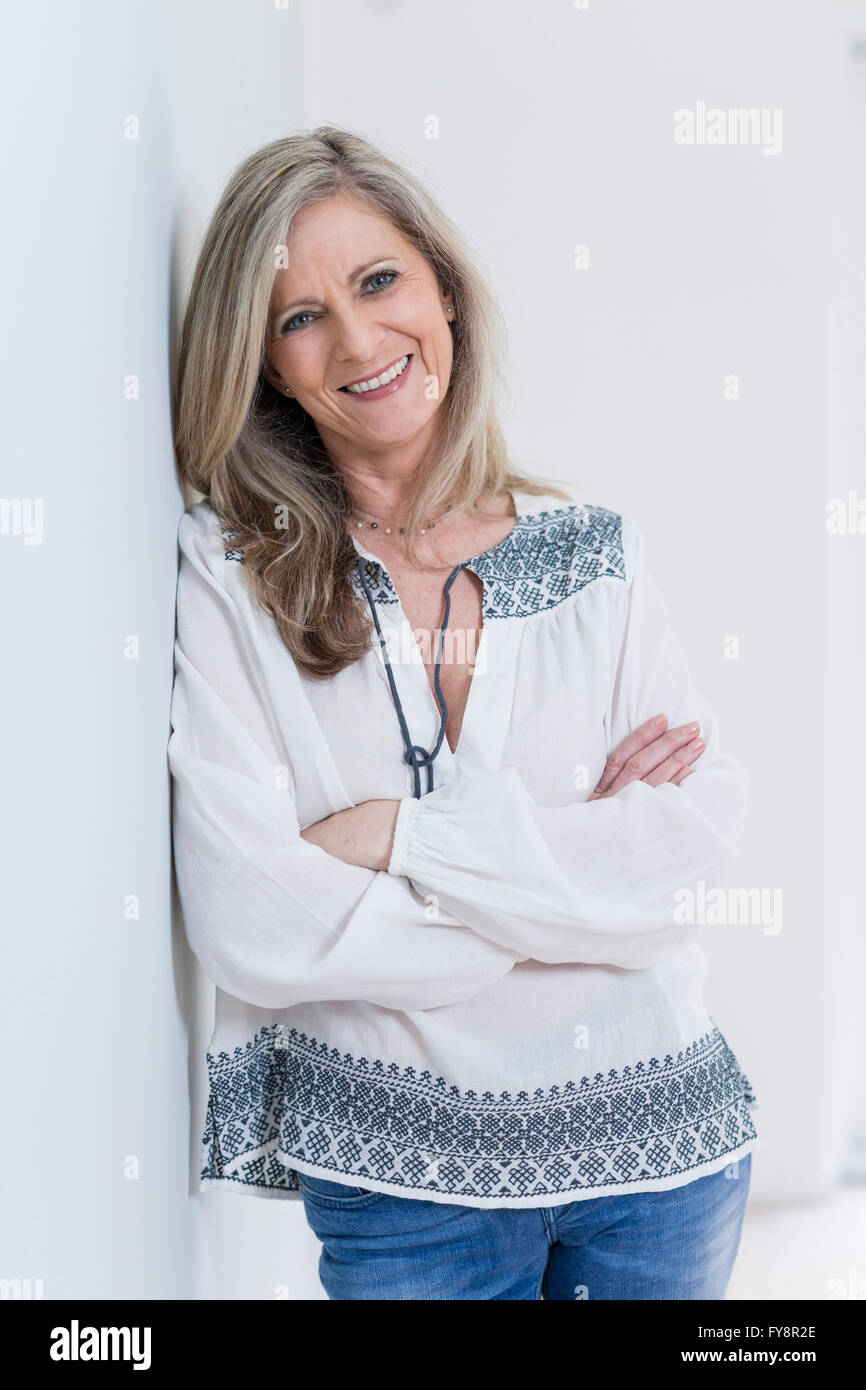 Portrait Of Smiling Blond Woman With Arms Crossed Leaning Against Wall