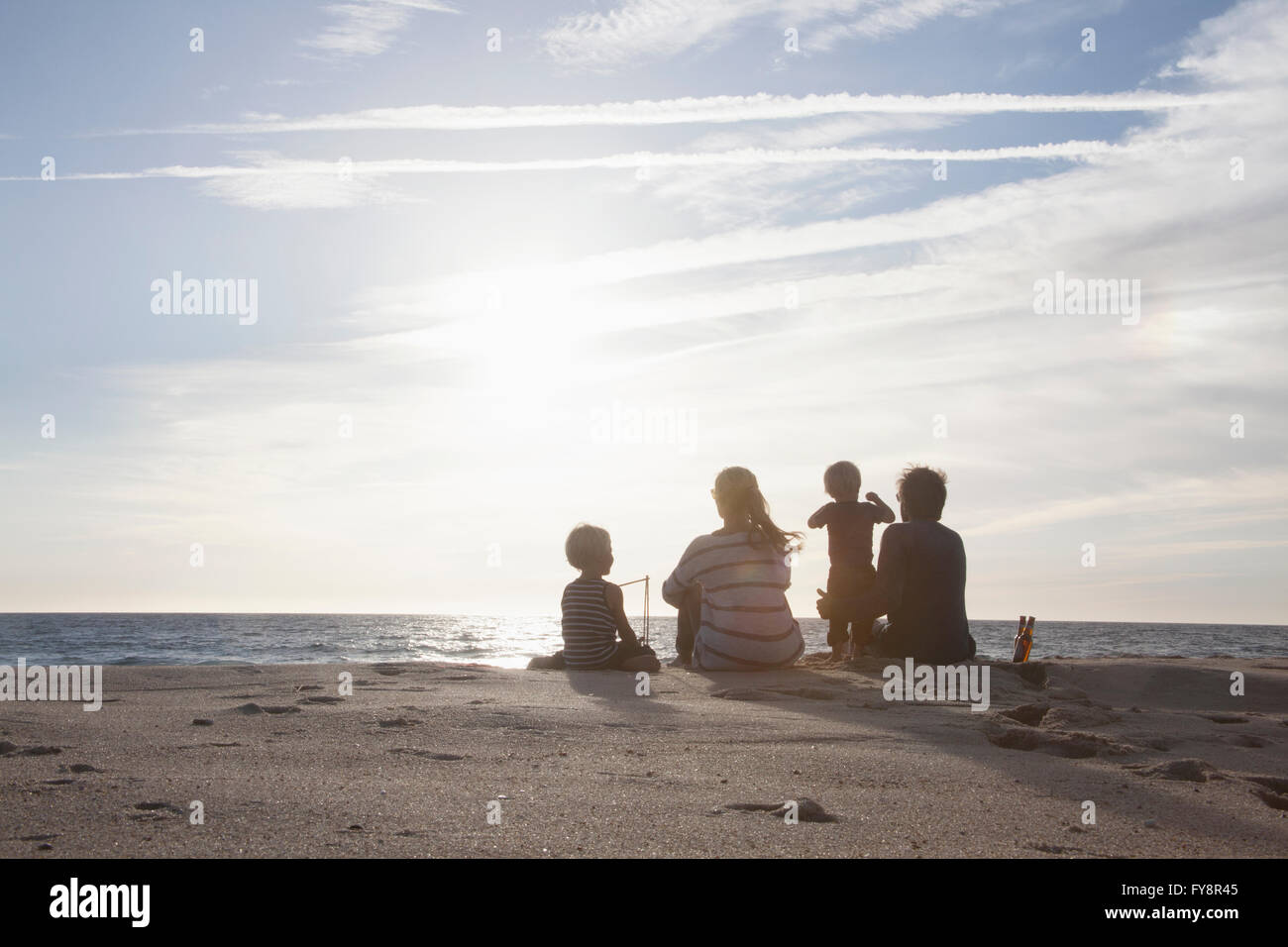 Back view of familiy with two kids sitting on the beach at twilight ...