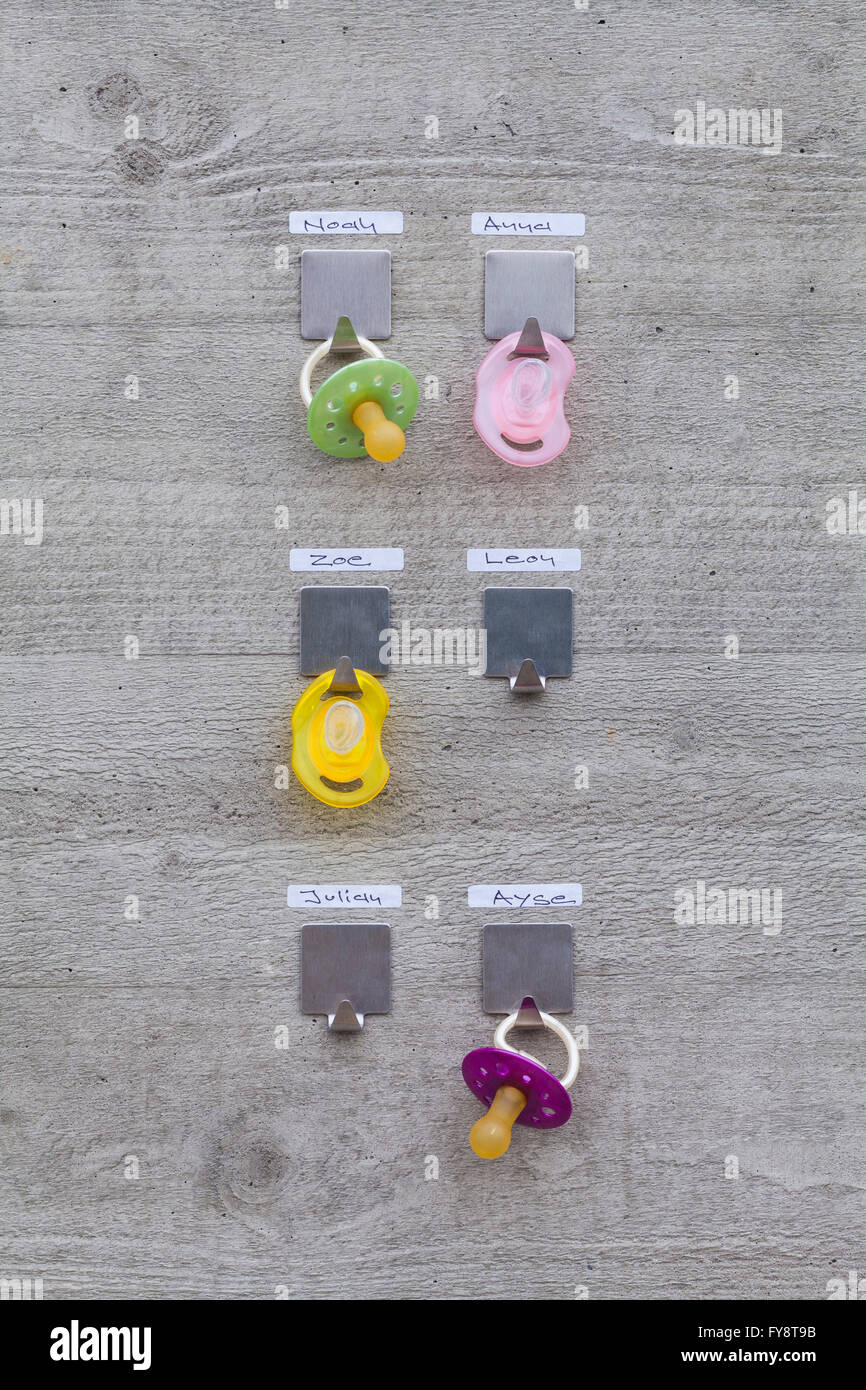 Pacifiers hanging on concrete wall with name tags Stock Photo - Alamy