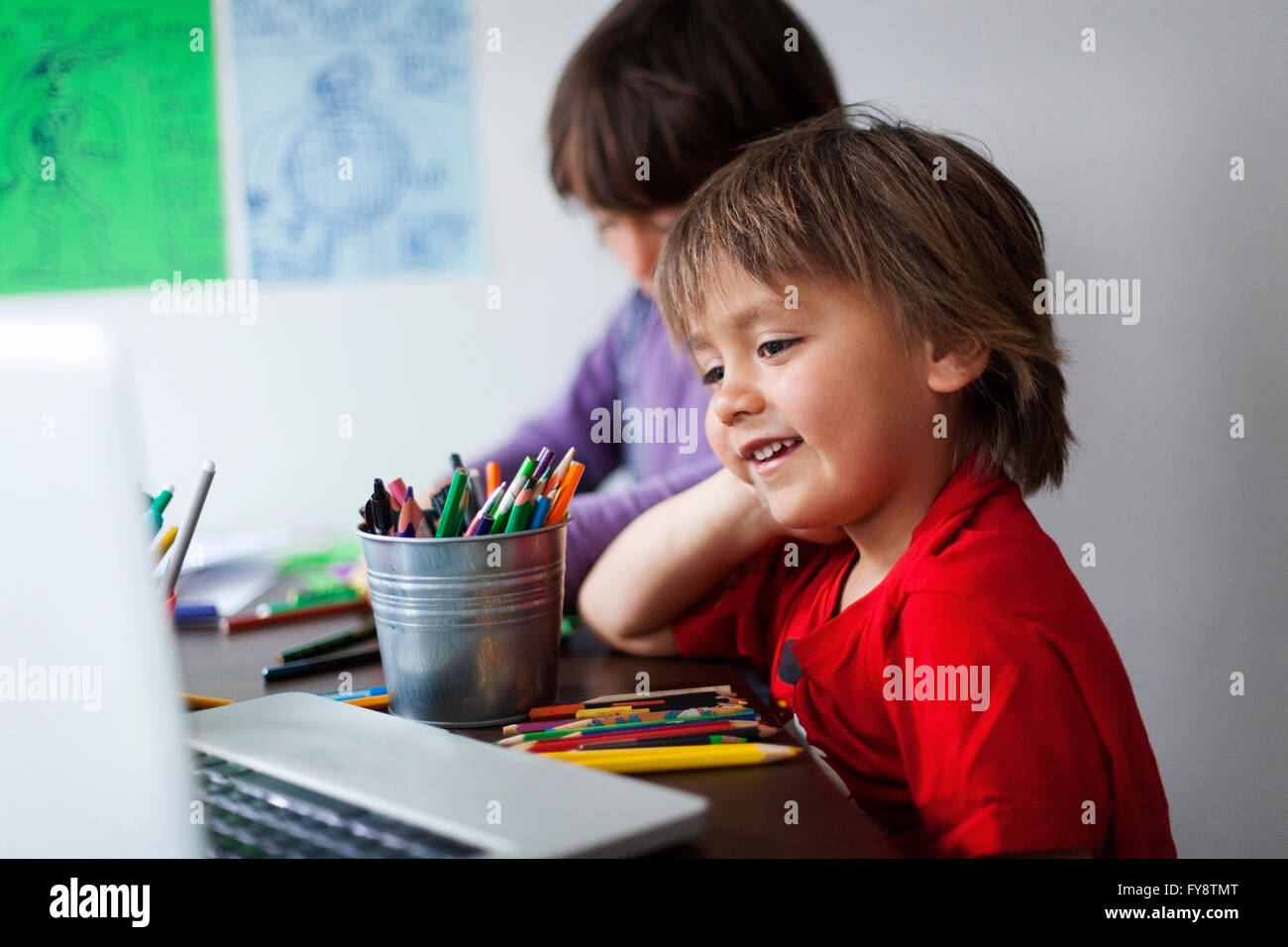 Portrait of smiling little boy watching a film at computer while his ...