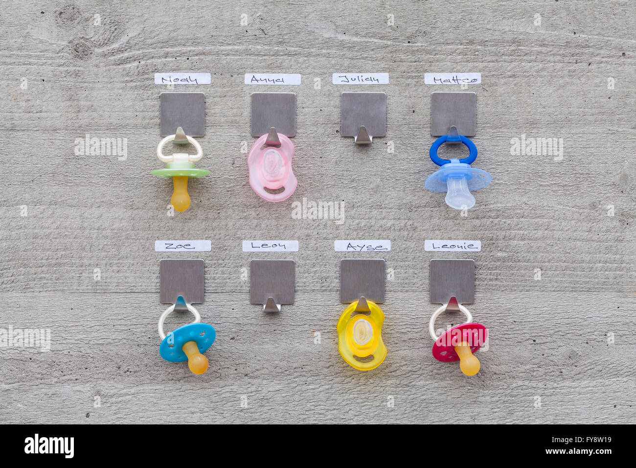 Pacifiers hanging on concrete wall with name tags Stock Photo - Alamy