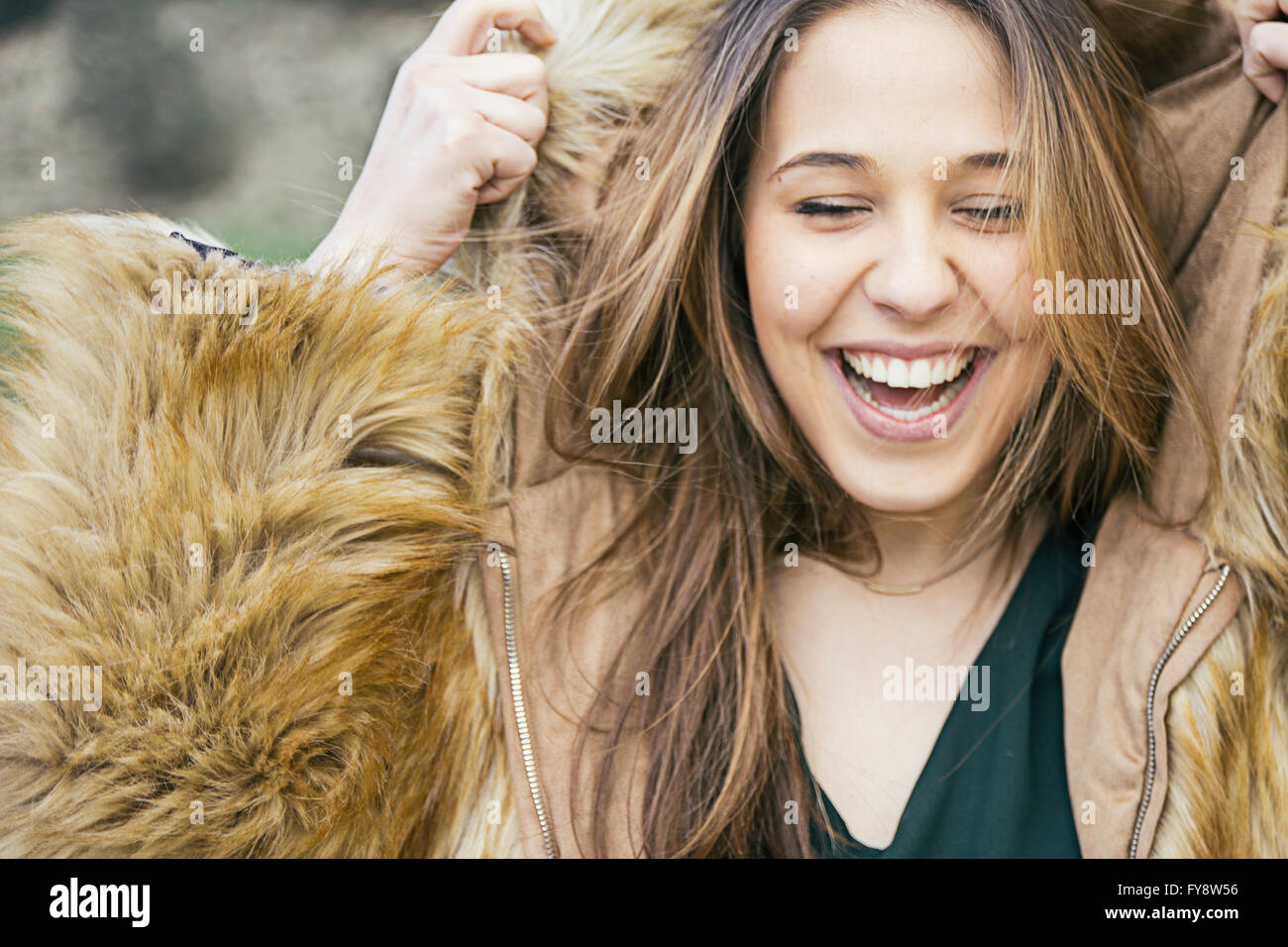 Portrait of laughing woman putting hood of a fur jacket on Stock Photo ...