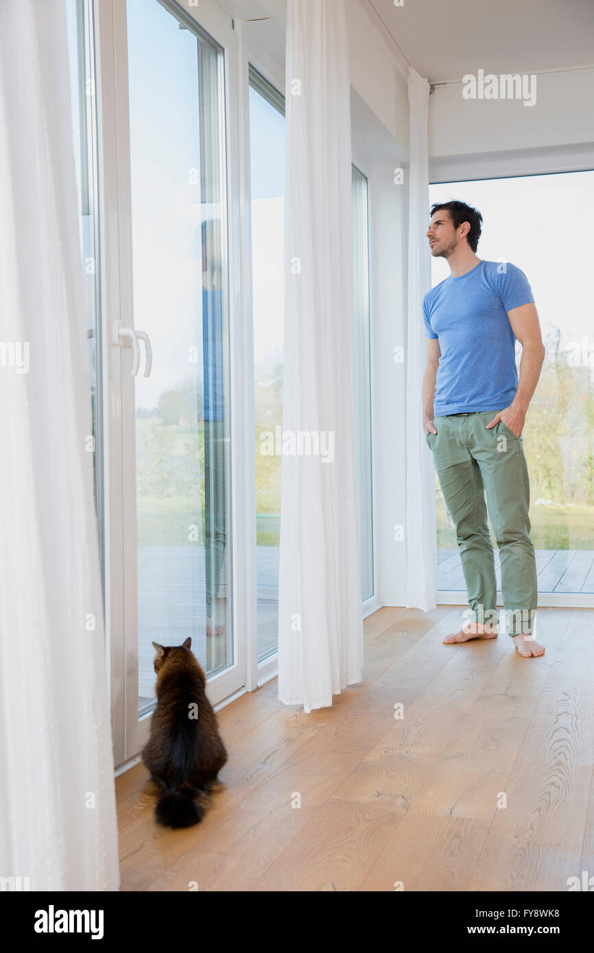 Man at home standing at window looking out Stock Photo - Alamy