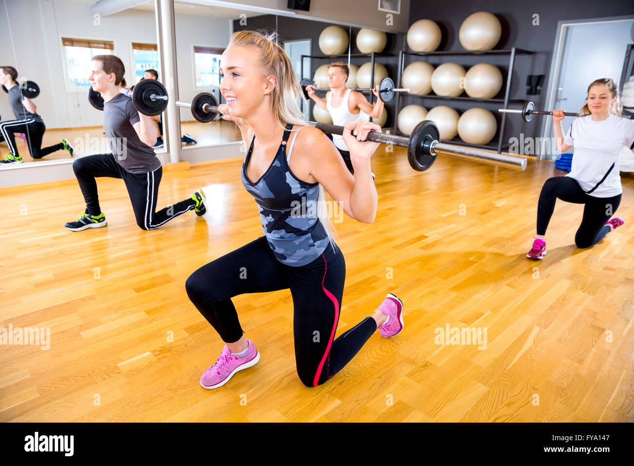 Smiling team doing split squats with weights at fitness gym Stock Photo ...
