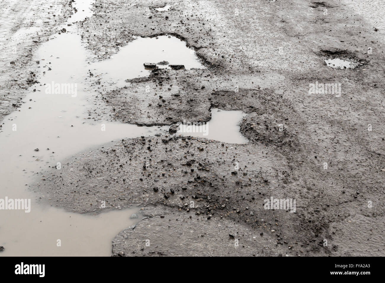 Large potholes in a broken tarmac road filled with muddy rainwater ...