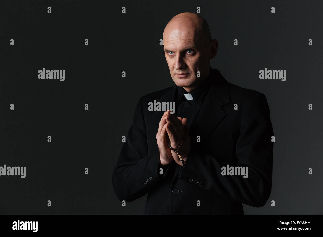 Priest standing and praying over black background Stock Photo - Alamy