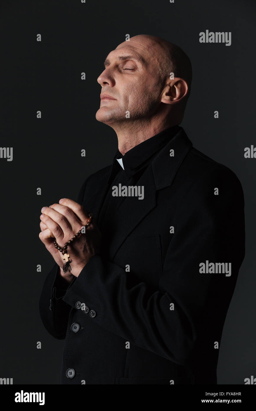 Priest with rosary praying with eyes closed over black background Stock ...