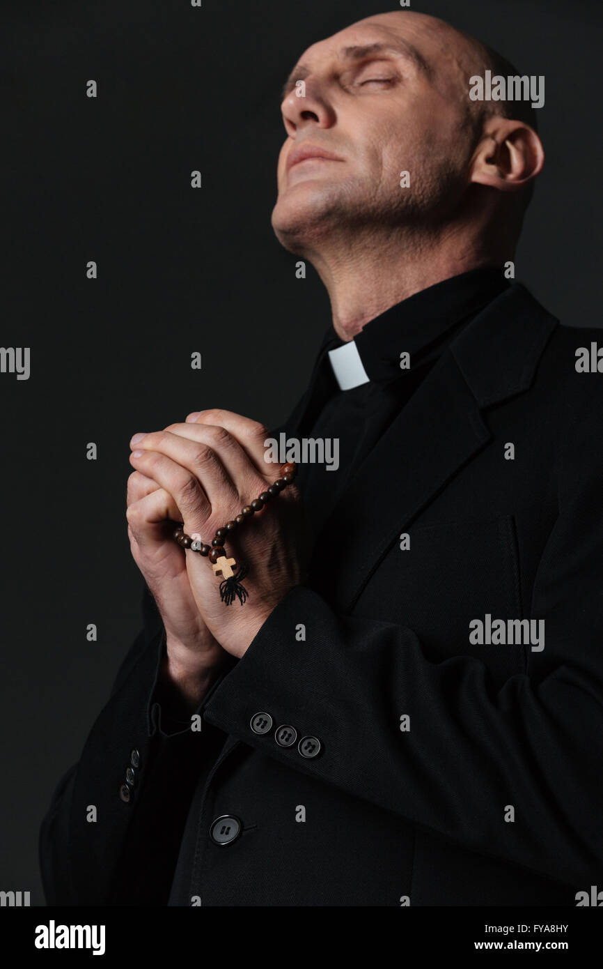 Priest standing with eyes closed and praying over black background ...