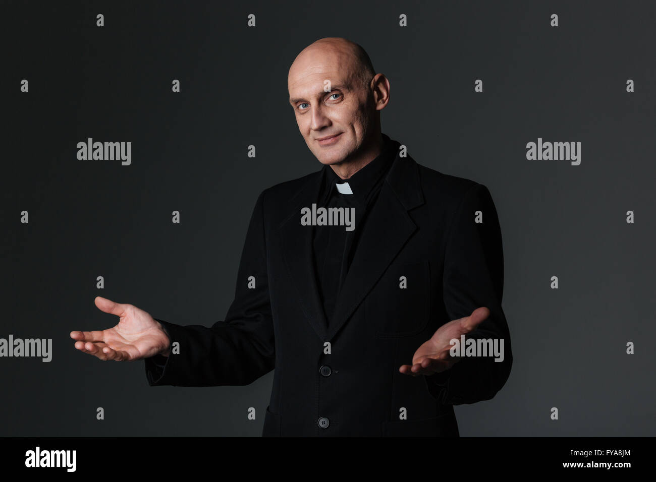 Smiling priest standing and inviting you over black background Stock ...