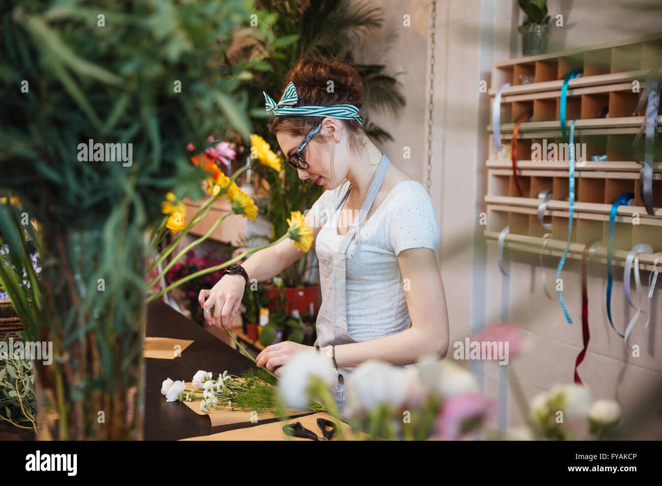 Serious pretty young woman florist standing and making bouquet with ...