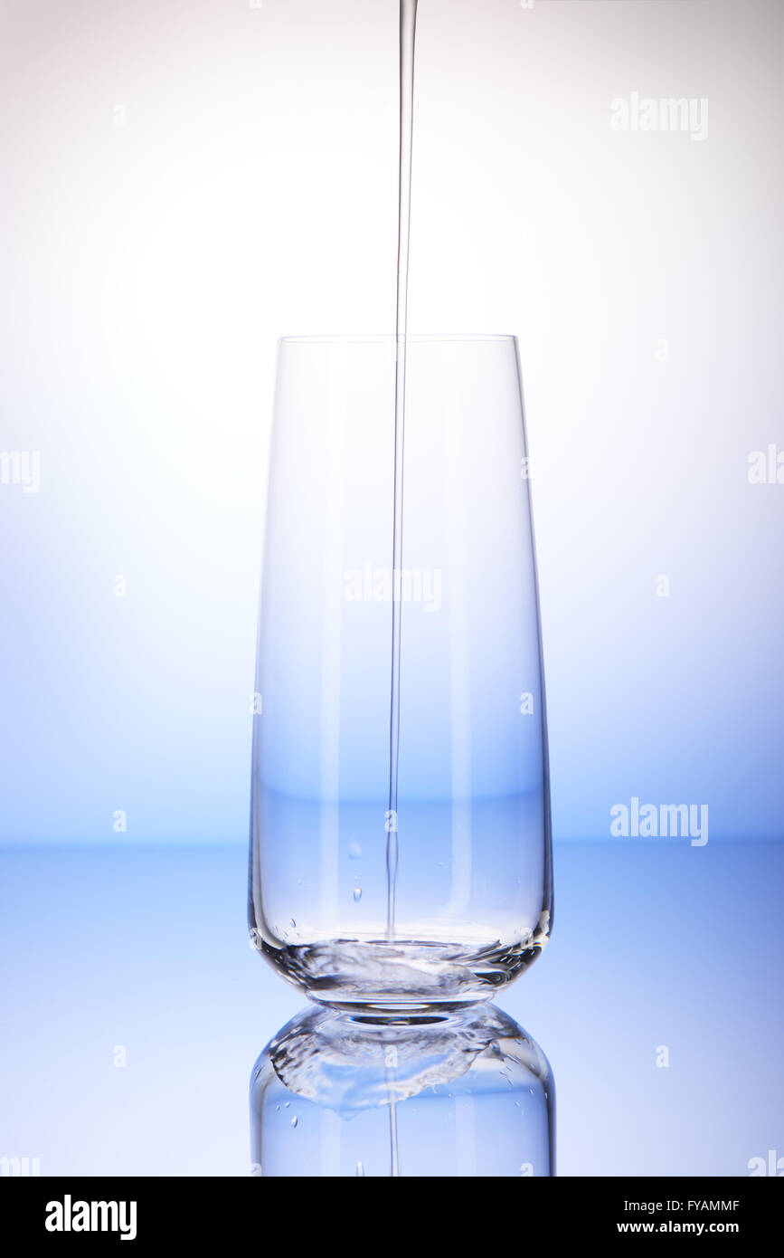 Water pouring into empty drinking glass with reflection on white and ...