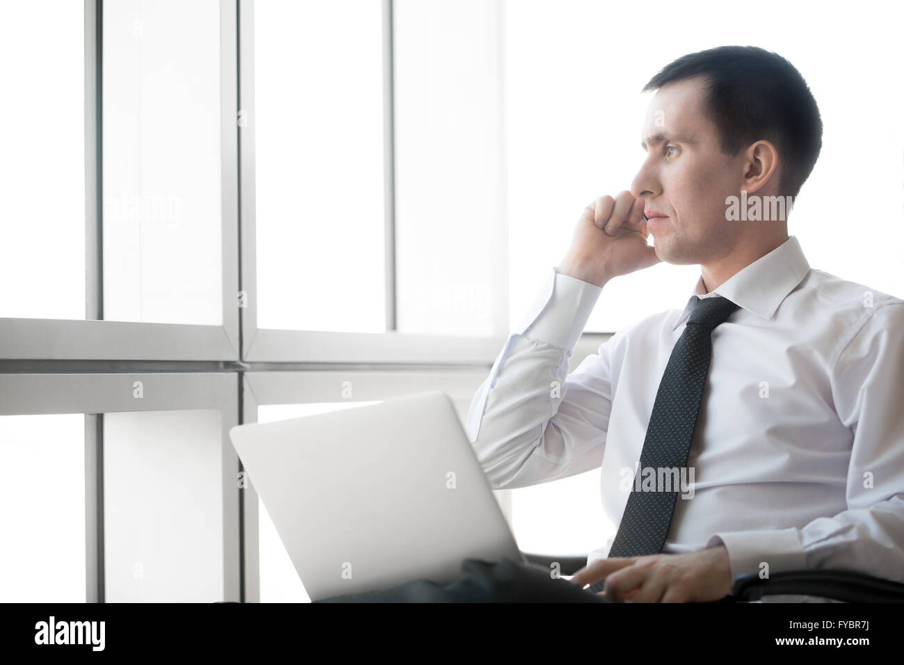 Portrait of serious handsome young business man working on laptop ...