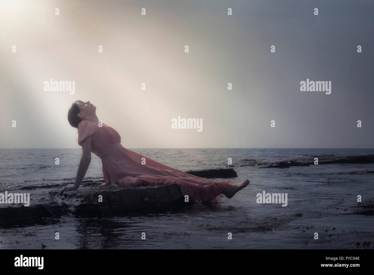 a woman in a pink dress is lying on stones at the sea Stock Photo - Alamy